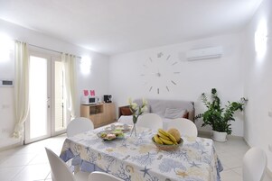 Uma sala de jantar com uma mesa posta para refeição, um relógio na parede e um vaso de planta.
