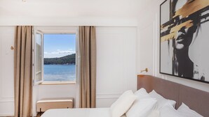 Quarto de hotel com cama, um banco, janela com cortinas e uma grande pintura abstrata na parede.