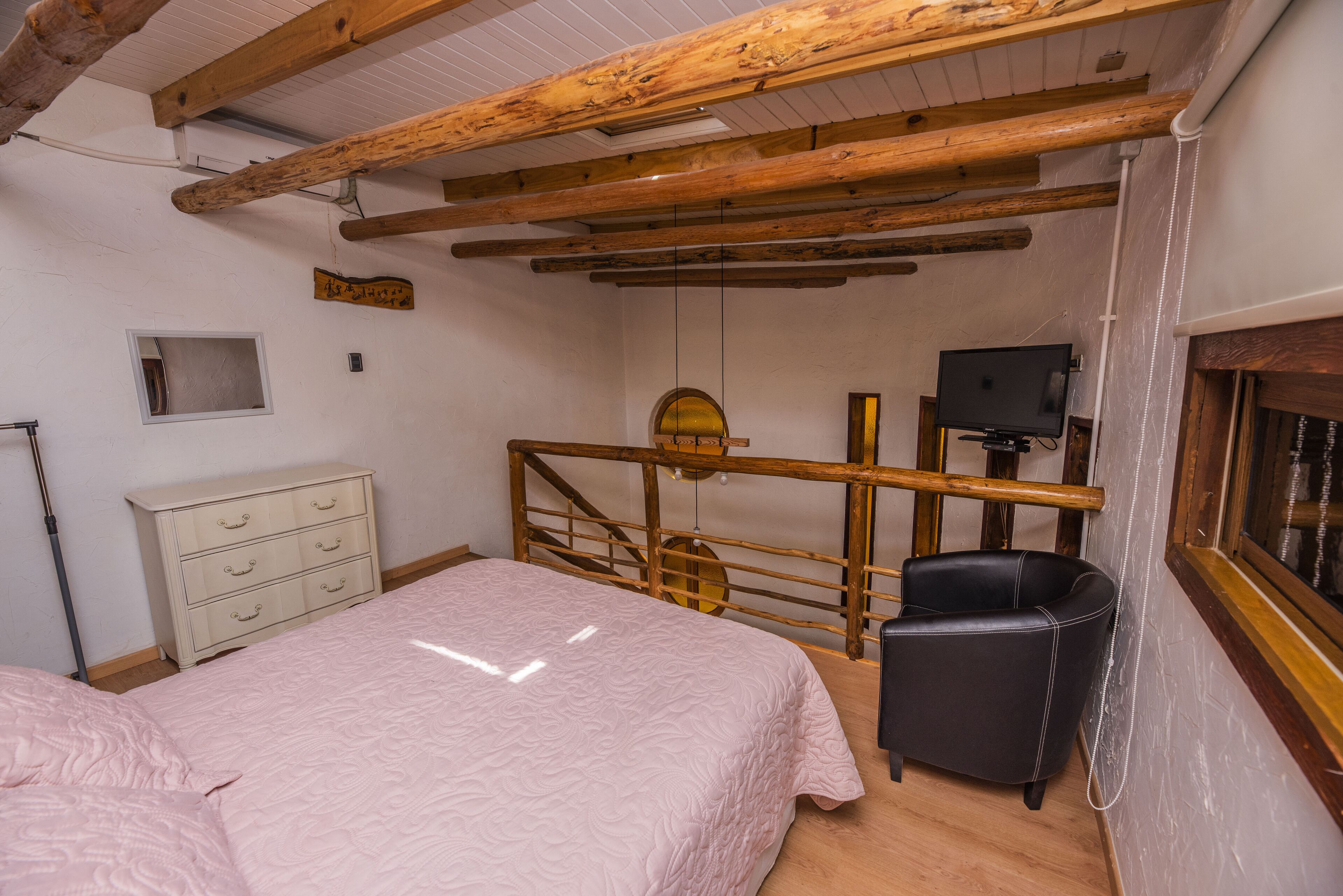 Um quarto com cama, cômoda, poltrona, televisão e vigas de madeira no teto.