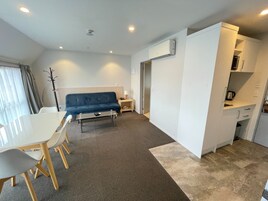 Uma sala de estar moderna com um sofá azul, uma mesa de jantar com cadeiras, uma mesa de centro e uma área de cozinha com micro-ondas e armários.