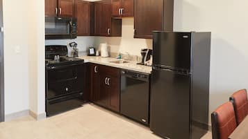 Uma cozinha compacta com armários de madeira escura, micro-ondas preto, geladeira preta e lava-louças.