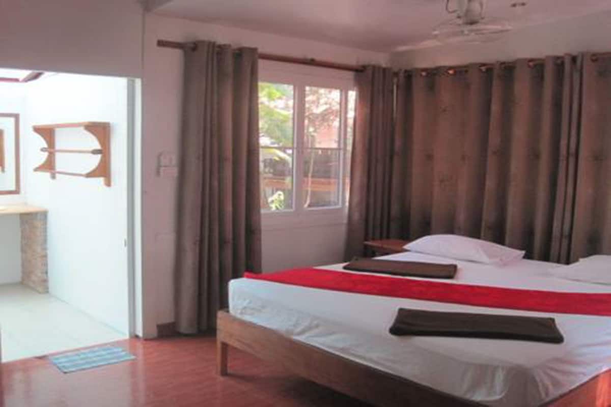 Quarto com cama de madeira, roupa de cama branca, manta vermelha e janela com cortinas.