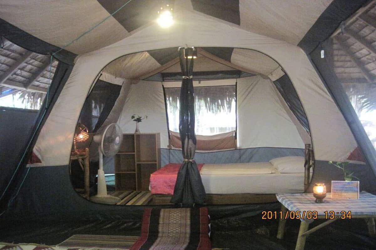 Uma tenda com uma cama, um ventilador e uma mesa com uma vela.