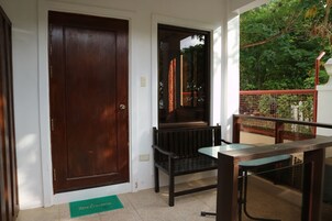 Uma porta de madeira, um banco, uma mesa de vidro e um corrimão vermelho.