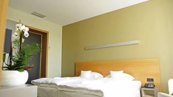 Quarto de hotel moderno com uma cama grande, uma mesinha de cabeceira e um vaso de planta.