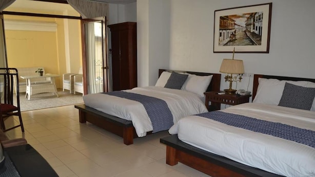 Quarto de hotel com duas camas, uma escrivaninha e uma cadeira. Tem uma varanda com mesa e cadeiras.