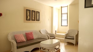 Uma sala de estar com sofá, duas poltronas, mesa de centro de vidro e janela com luz natural.