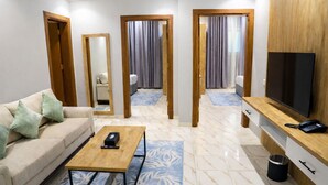 Quarto de hotel moderno com sofá, mesa de centro, televisão e secretária com telefone.