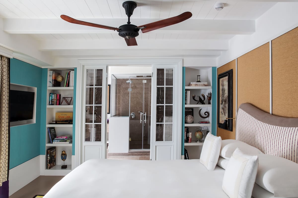 Quarto com cama, ventoinha no teto, televisão e banheiro com chuveiro.