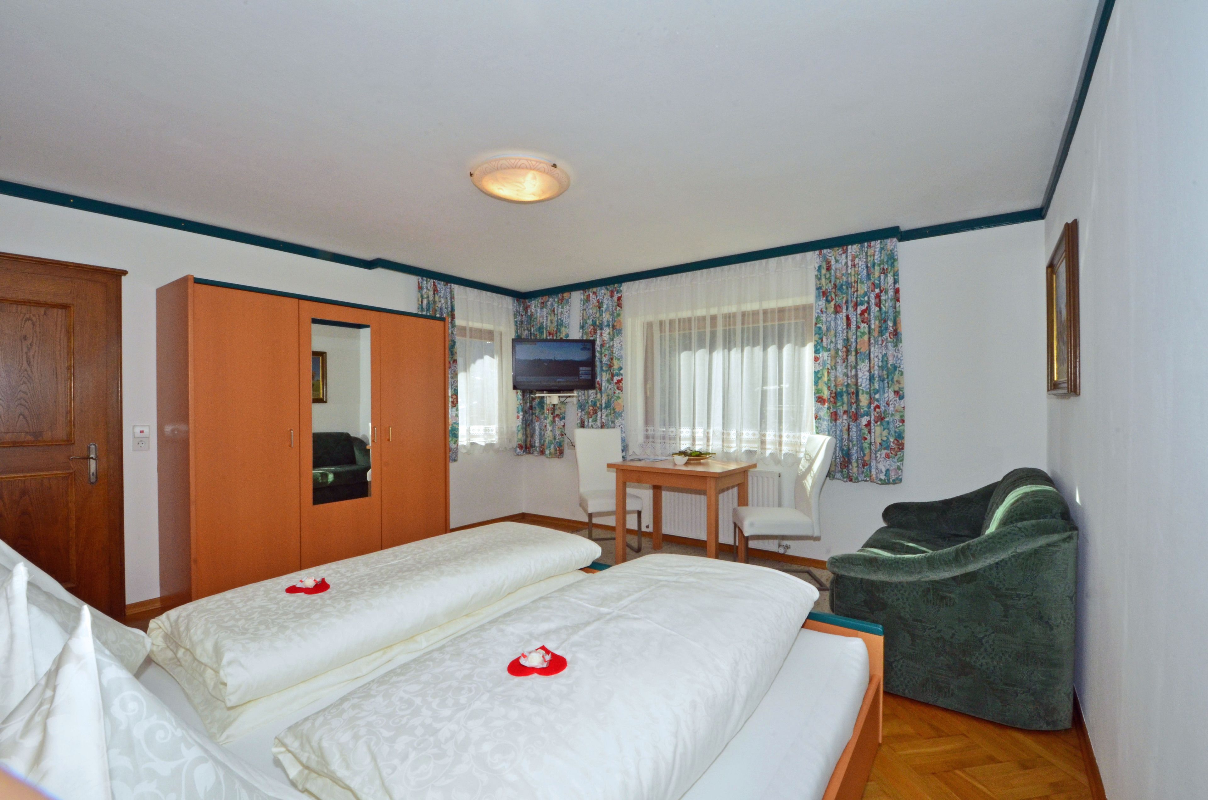 Quarto de hotel com duas camas, uma escrivaninha, uma televisão e uma poltrona verde.