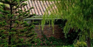 Um edifício com telhado de cerâmica, rodeado por vegetação e um muro de tijolos.