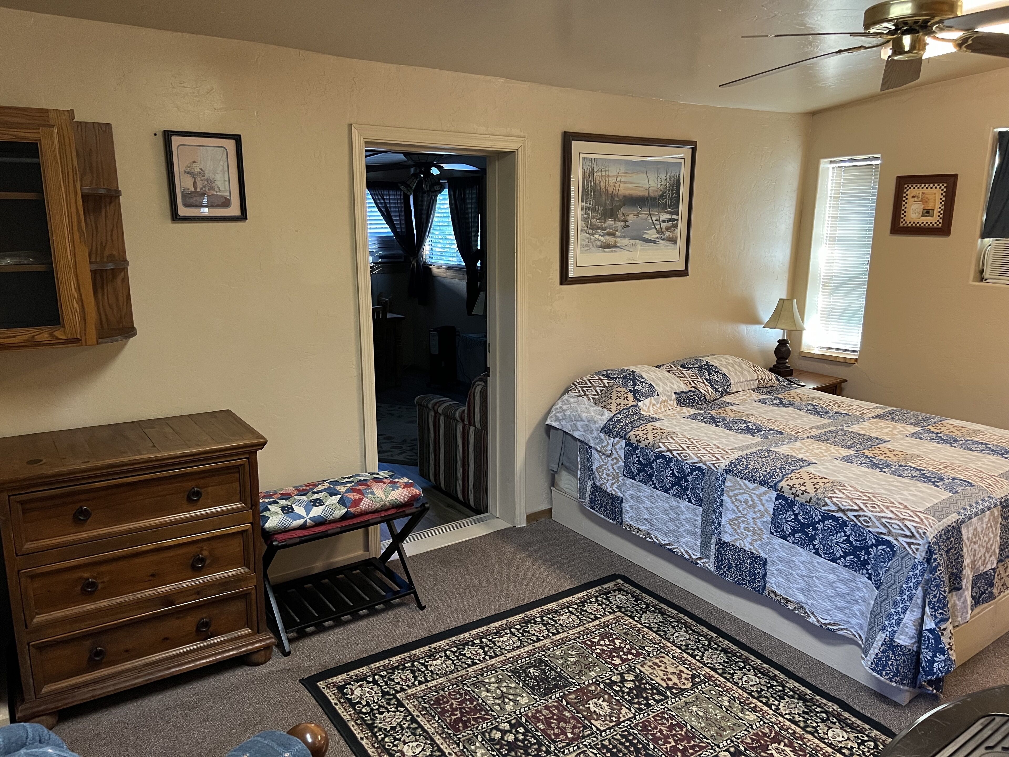 Quarto com cama, penteadeira, cadeira e porta para outro cômodo.