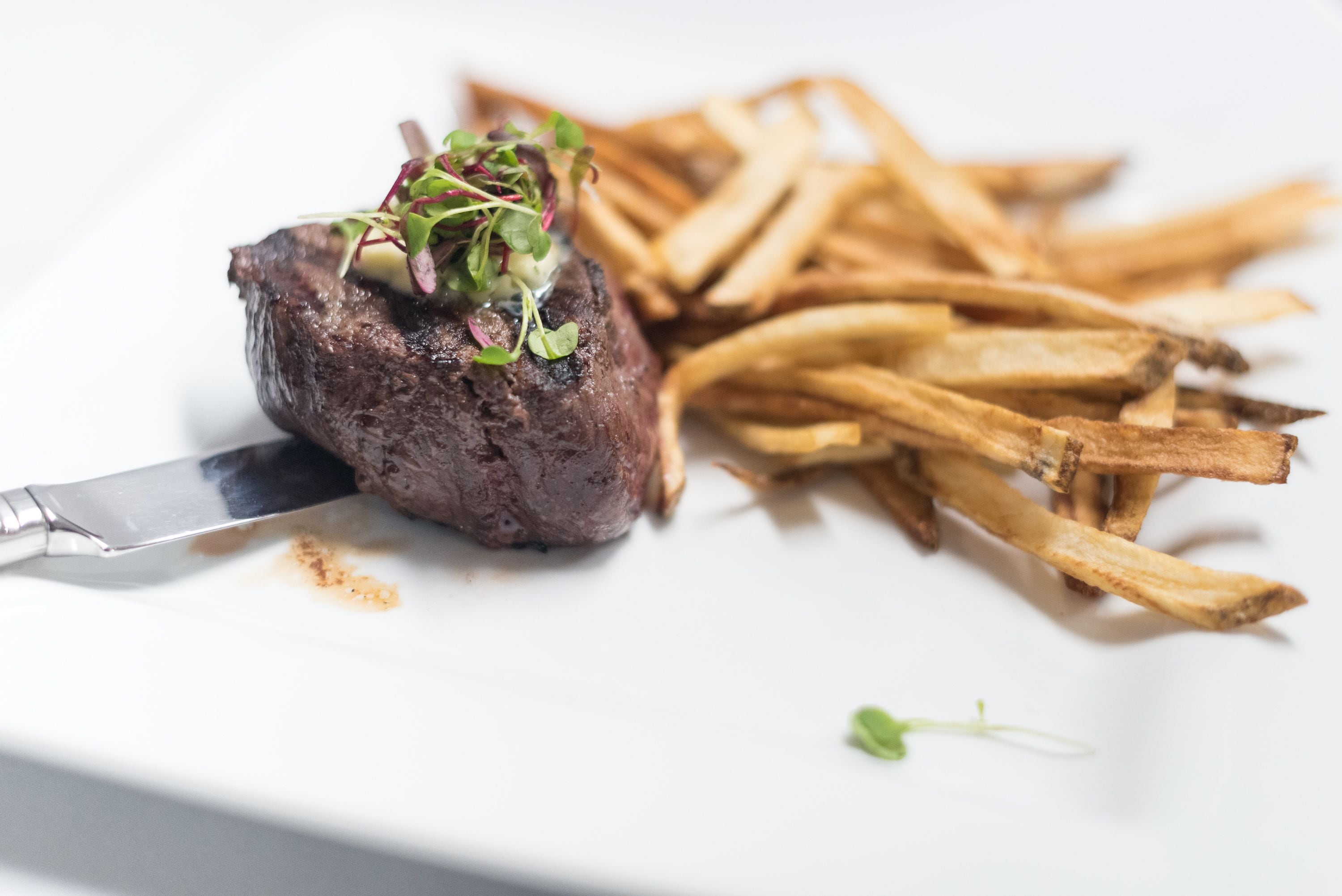 Bife com faca em um prato, acompanhado de batatas fritas.