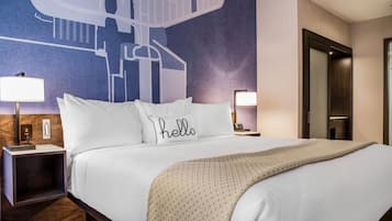 Quarto de hotel com uma cama grande, duas mesas de cabeceira com luminárias, um mural na parede e uma porta.