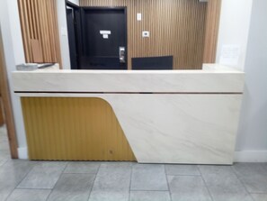 Balcão de recepção com painel de madeira e bancada de mármore.