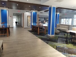 Um hall de hotel com um corredor extenso, áreas de estar e uma mesa de recepção.