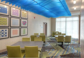 Uma sala de conferências com mesas e cadeiras, obras de arte emolduradas na parede e um tapete estampado.