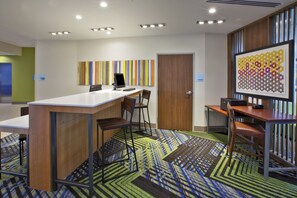 Um espaço de escritório moderno com uma mesa comprida, cadeiras, um computador e uma pintura abstrata colorida.