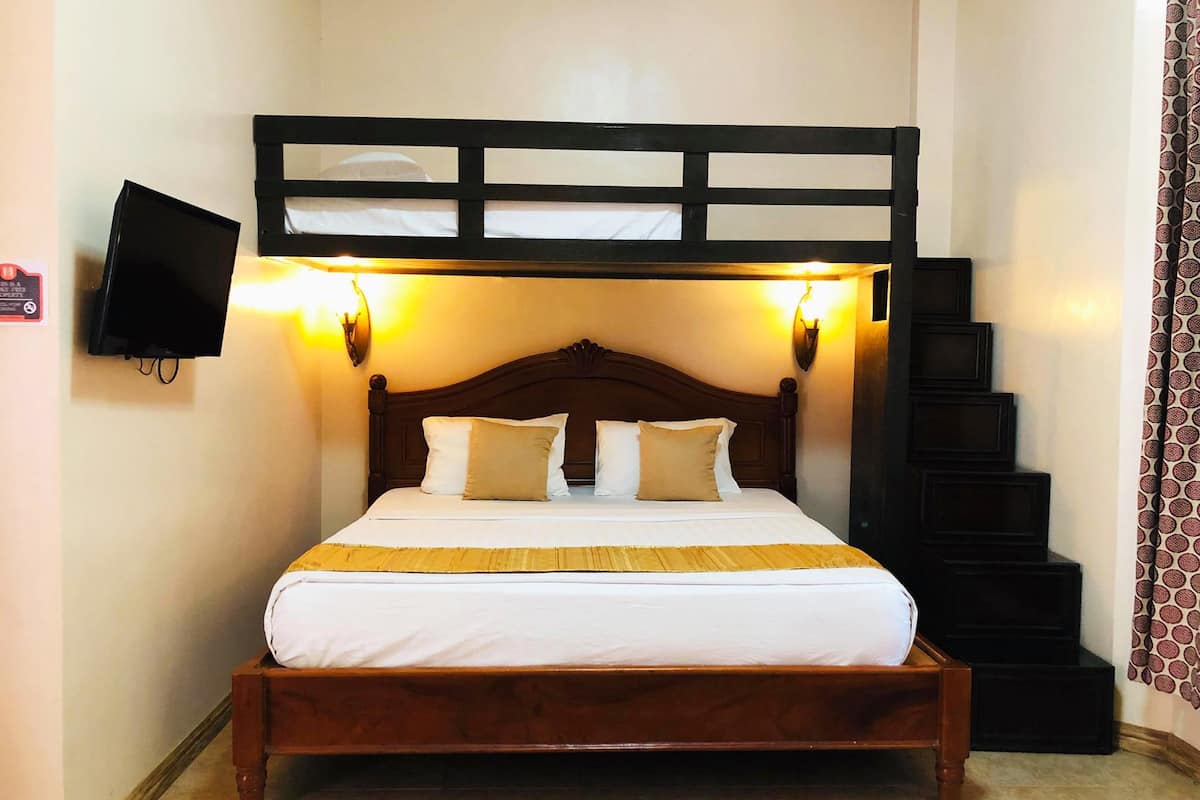 Uma cama com cabeceira de madeira, duas luminárias na parede e uma televisão fixada na parede.