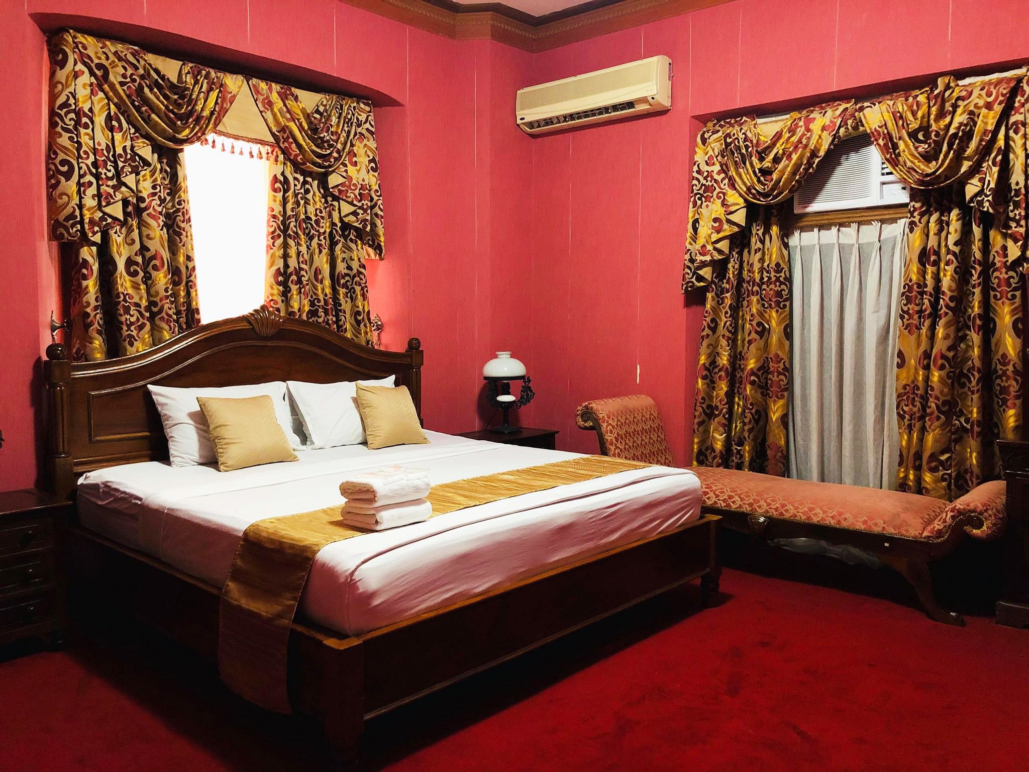 Quarto de hotel com cama grande, mesa de cabeceira, uma cadeira e janela com cortinas.