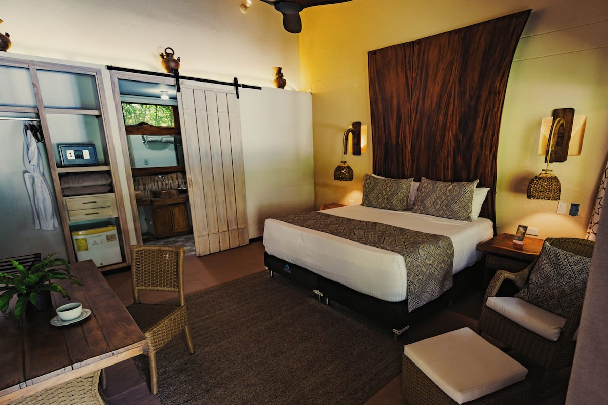 Quarto com cama, escrivaninha, cadeira, mesinha e um vaso de planta.