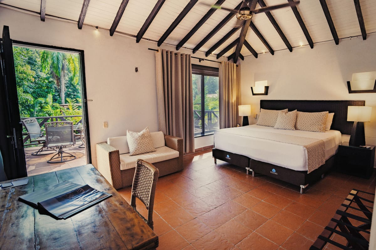 Quarto com cama grande, sofá, mesa de jantar e vista para o exterior.