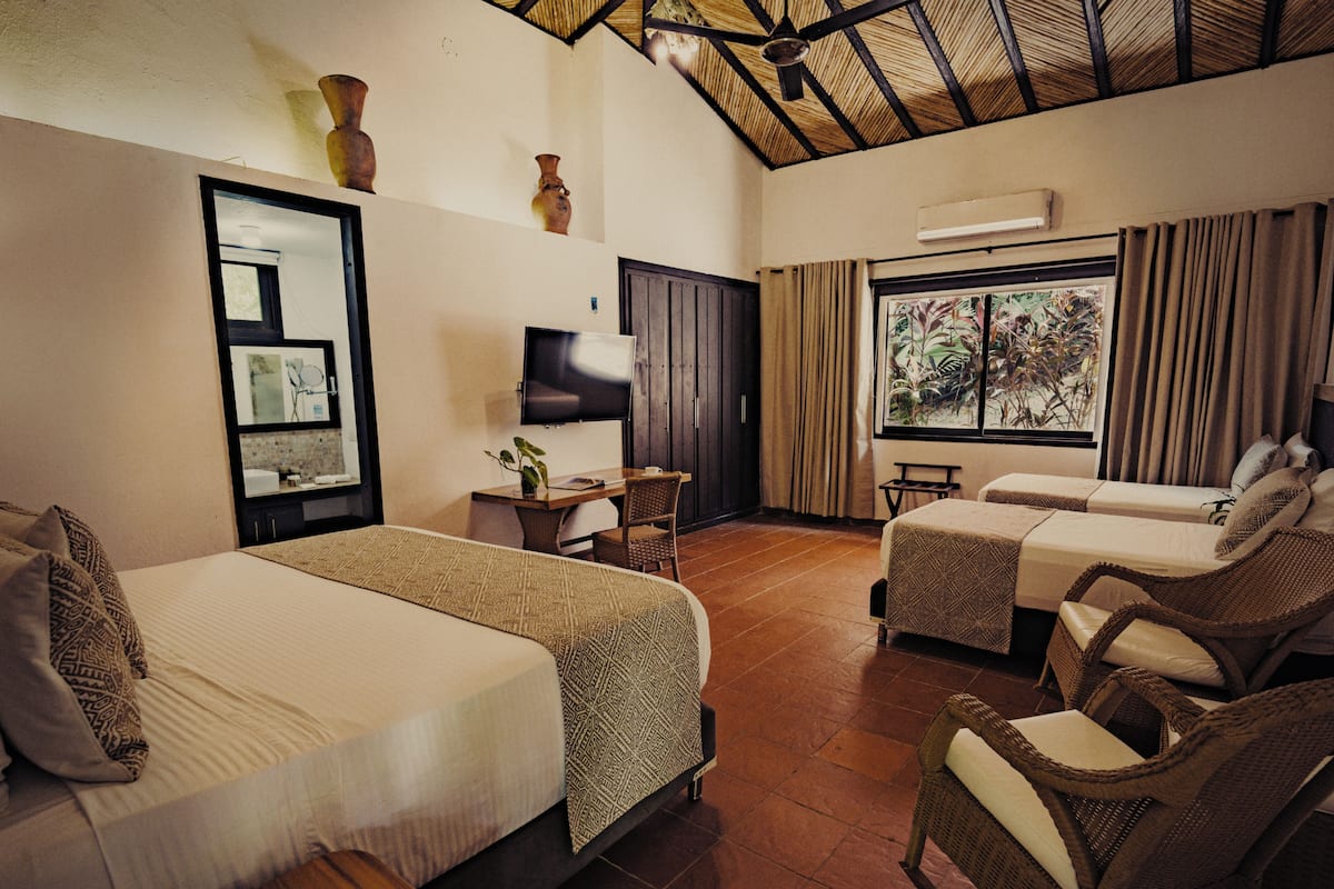 Quarto de hotel com duas camas, televisão, escrivaninha e uma janela grande.