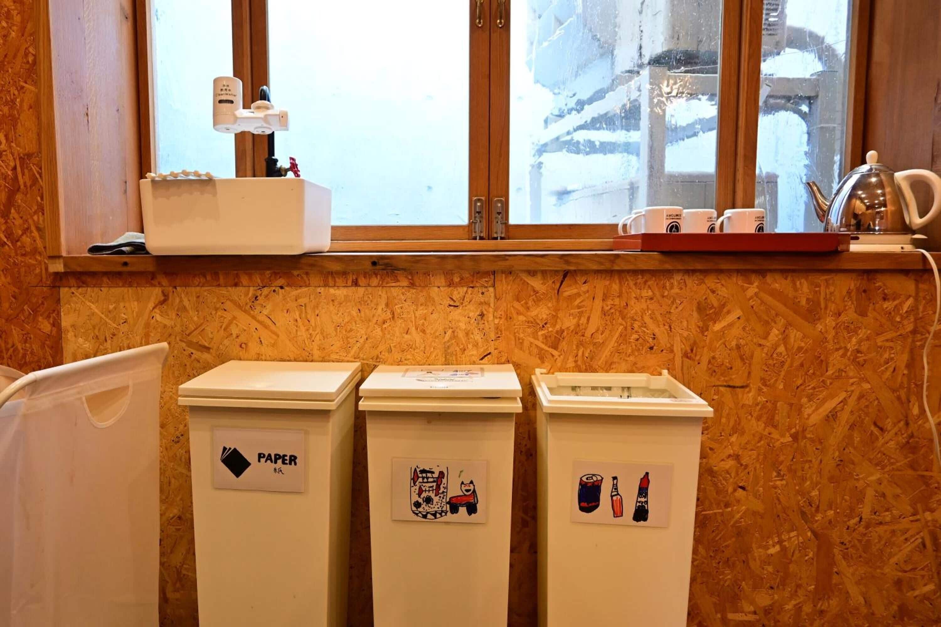 Cozinha com janela, parede de madeira e três lixeiras identificadas como 'PAPEL'.