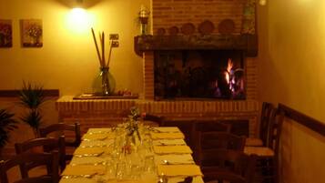 Uma sala de jantar com lareira de tijolos, uma mesa posta para quatro pessoas e um vaso com flores.