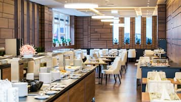 Uma sala de jantar moderna com serviço de buffet, várias mesas e um balcão longo com opções de comida e bebida.