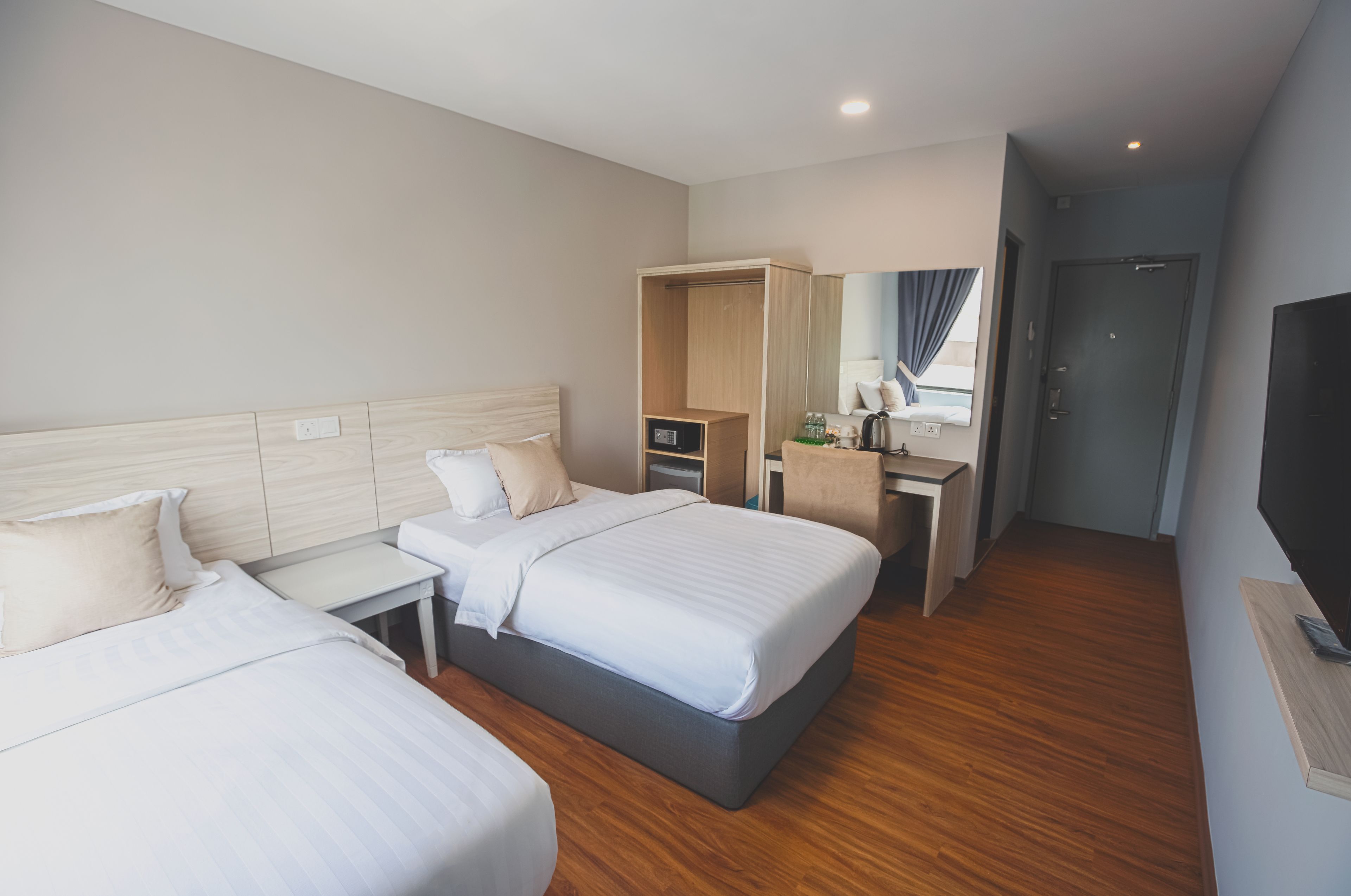 Quarto de hotel com duas camas, uma escrivaninha, um espelho e uma televisão.