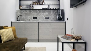 Uma cozinha compacta com máquina de café integrada, resfriador de vinhos e bancada com diversas garrafas.
