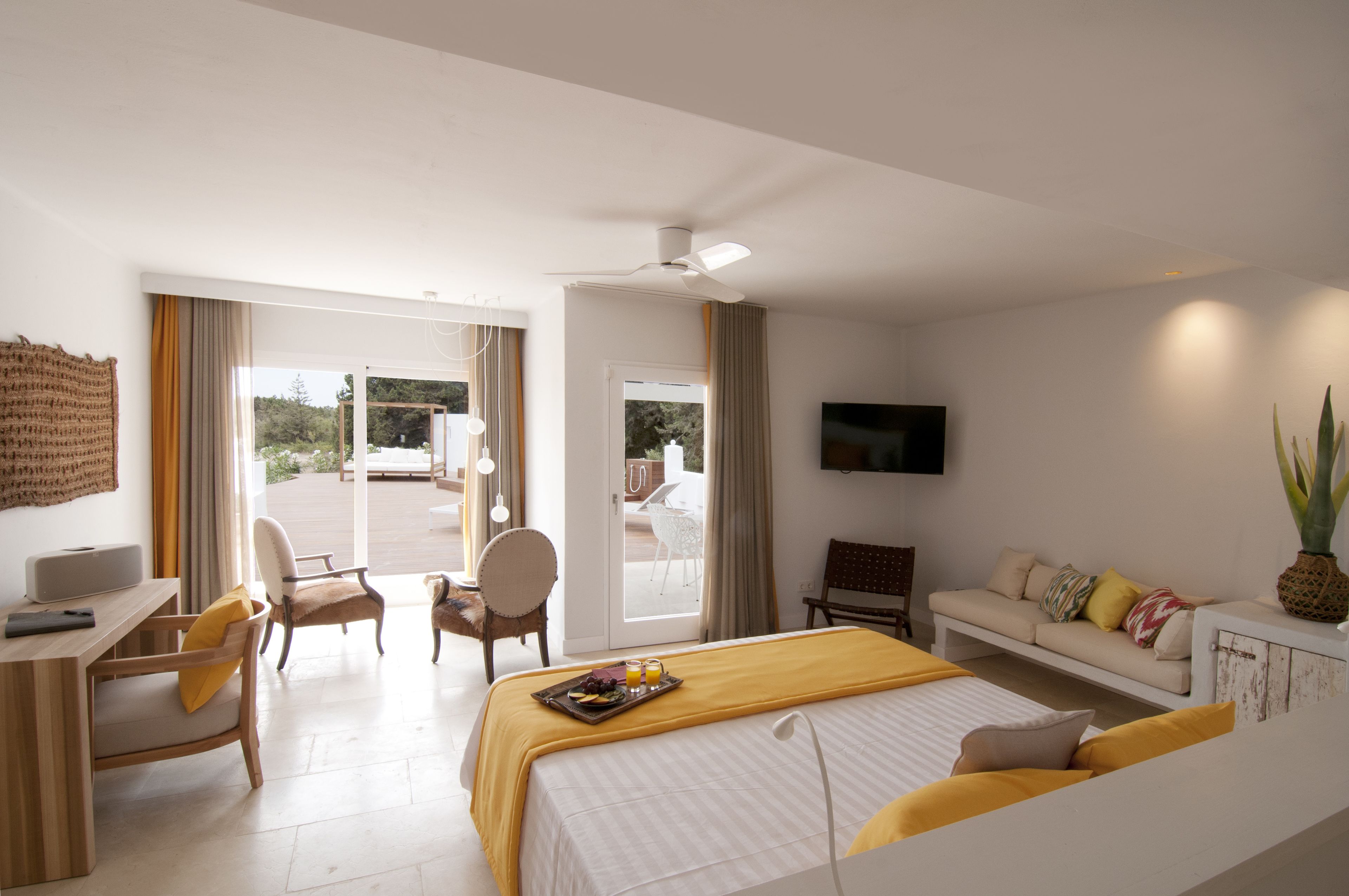 Quarto de hotel com cama, escrivaninha, cadeira, sofá e televisão.