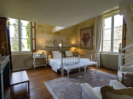 Quarto com cama, mesas de cabeceira, um rodapé, janela, radiador, piso de madeira e tapete estampado.