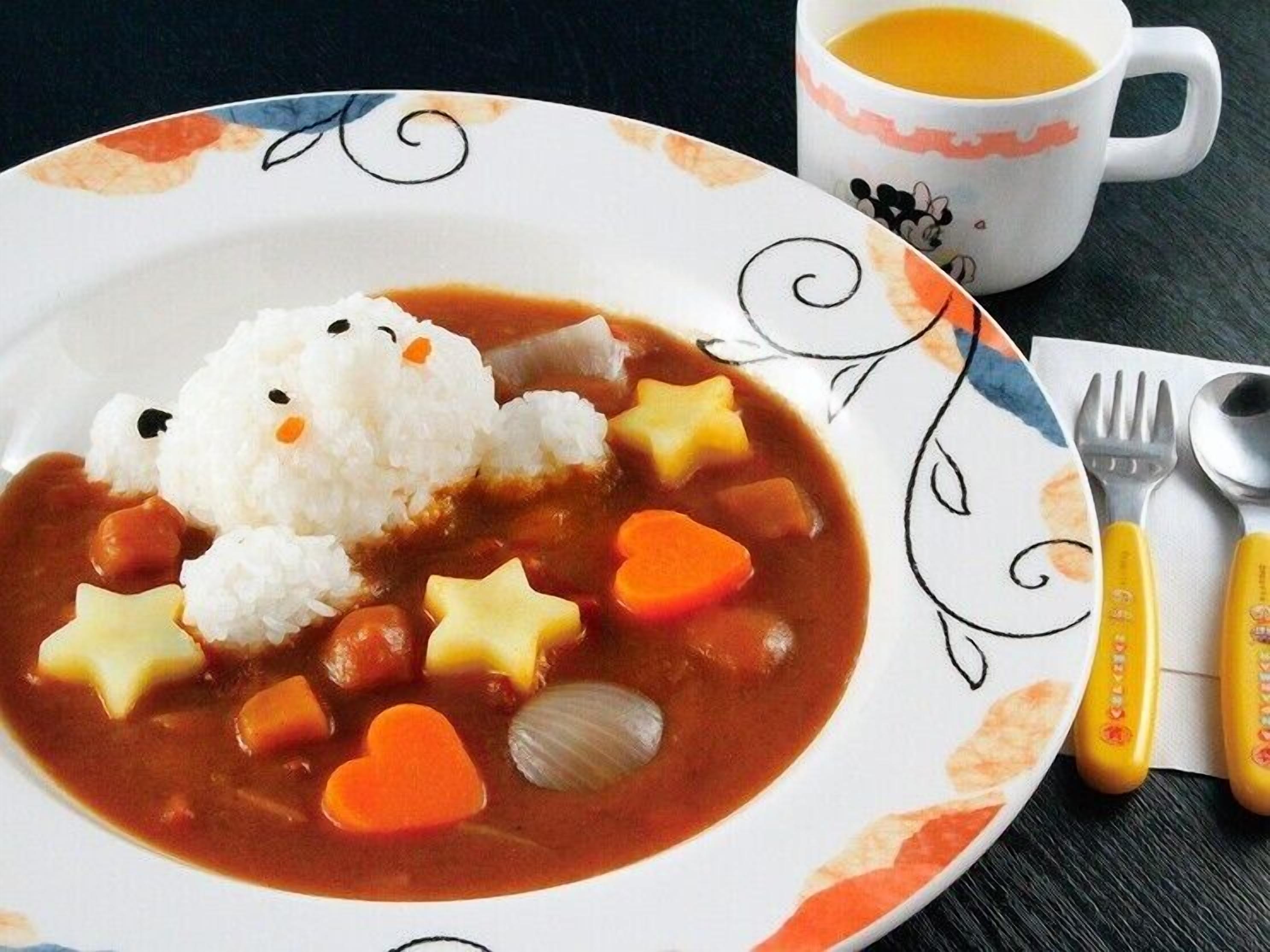 Uma tigela de sopa com arroz modelado como um boneco de neve, legumes em formato de estrela e uma xícara de chá ao lado.