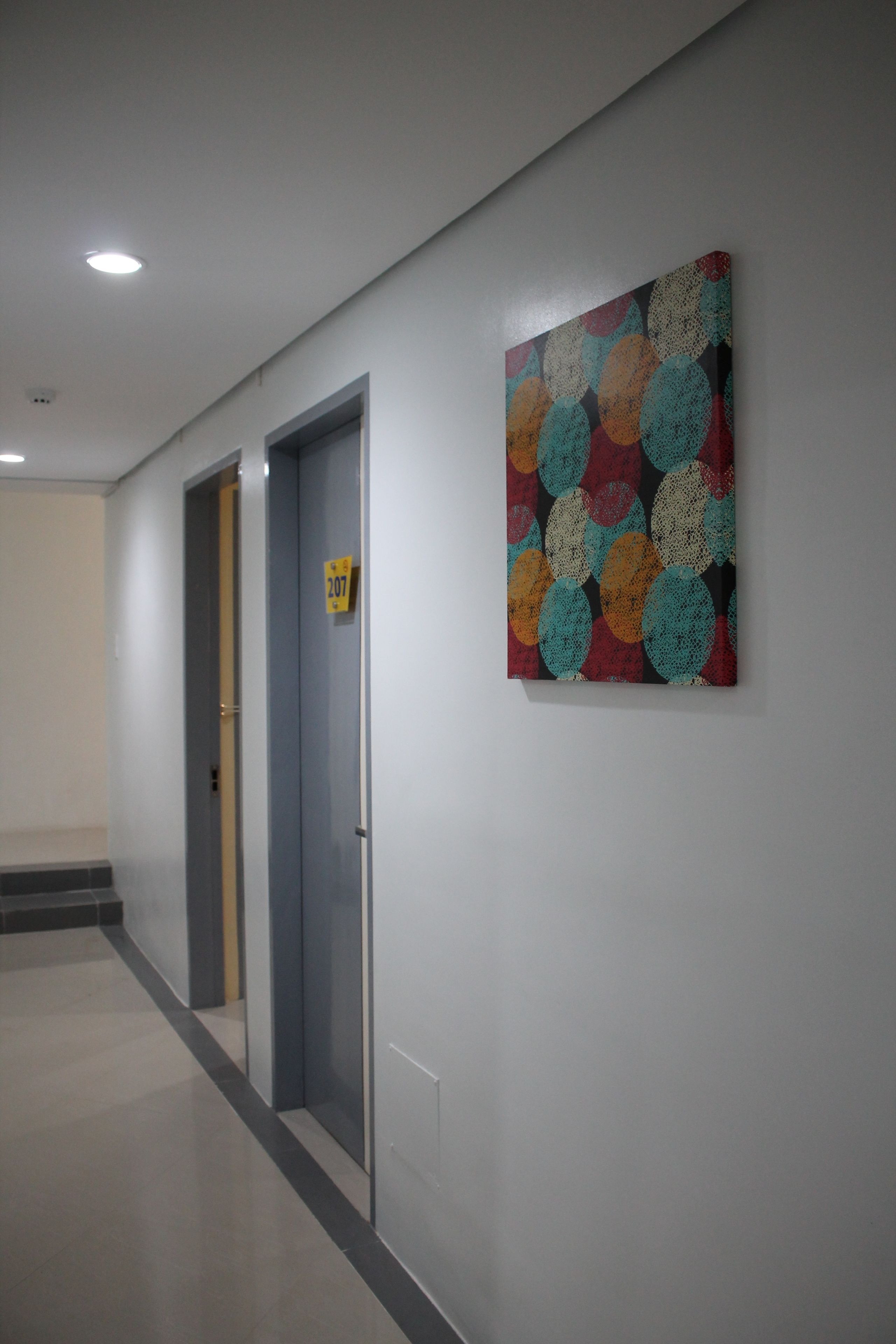 Um corredor com duas portas, uma delas com o número 207, e uma pintura abstrata colorida na parede.