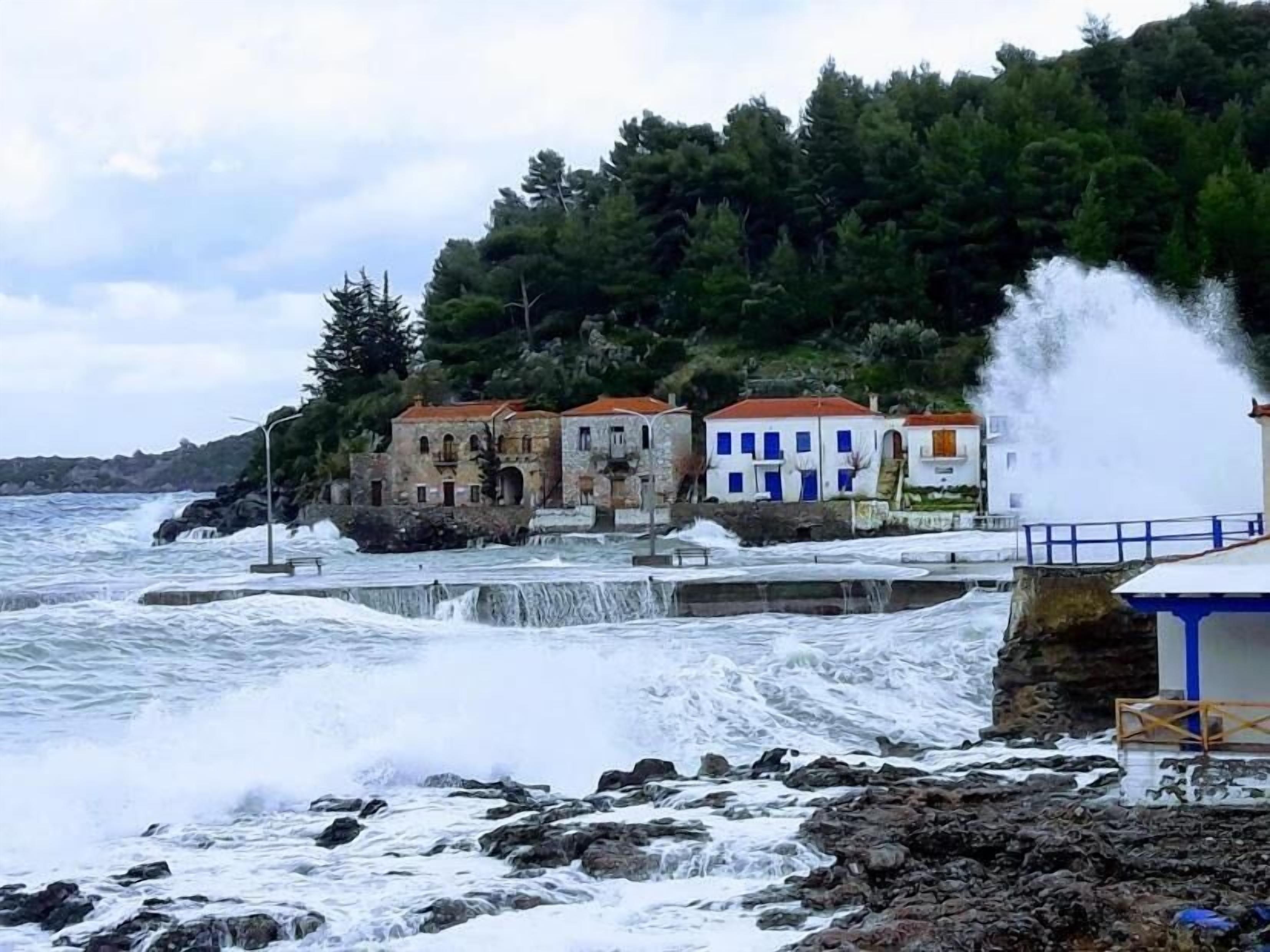 Uma paisagem costeira com margem rochosa, vários edifícios com arquitetura tradicional e um mar agitado.