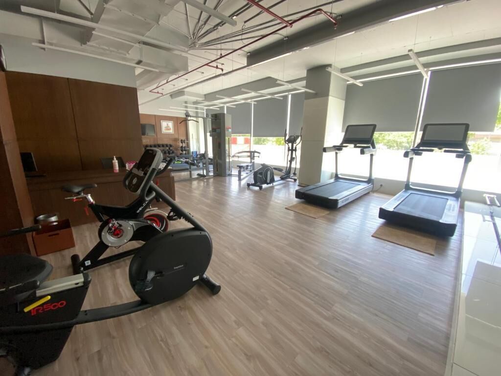 Uma academia com equipamentos de cardio, bancos de peso e piso de madeira.