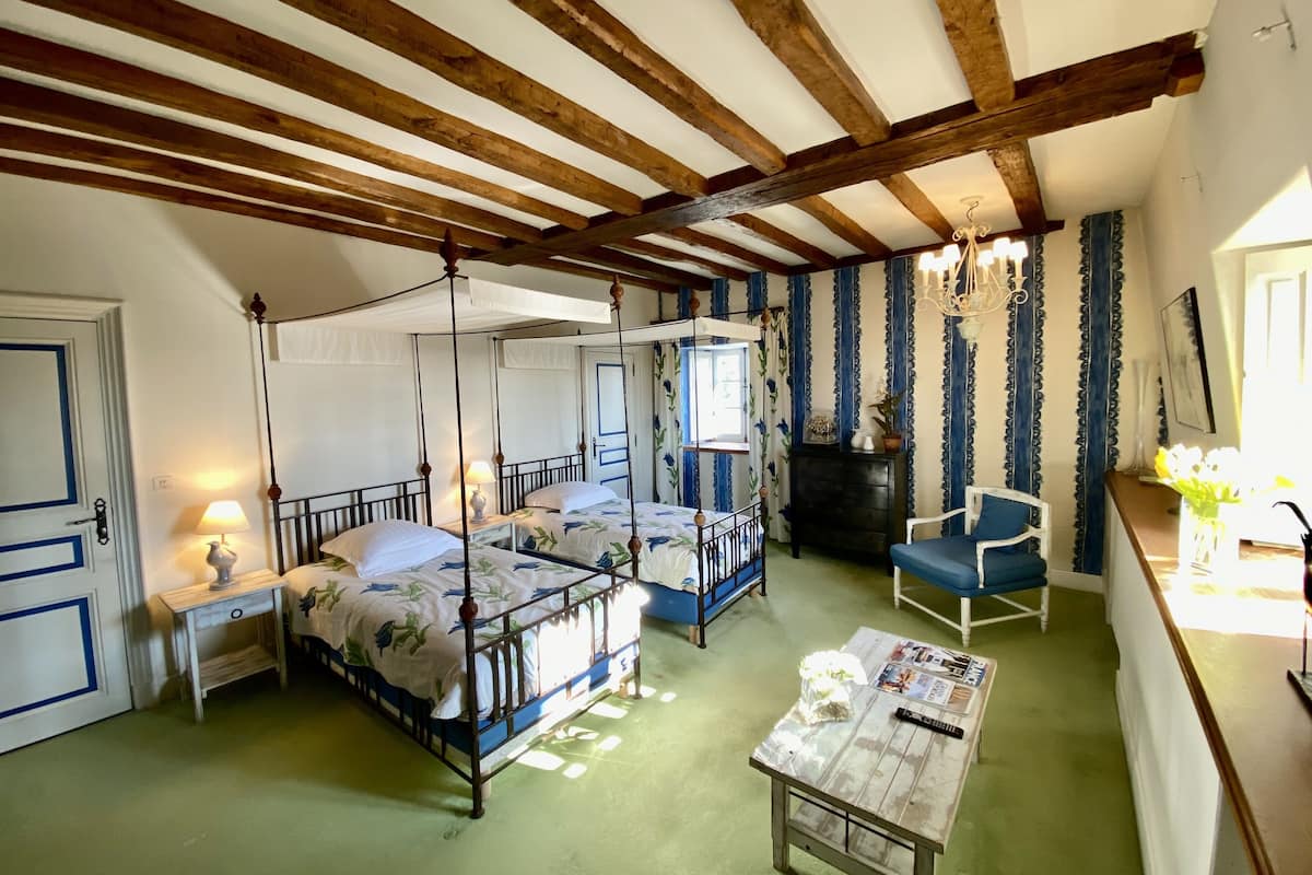 Quarto com cama de dossel, uma pequena mesa com um controle remoto, uma cadeira e teto de madeira com vigas aparentes.