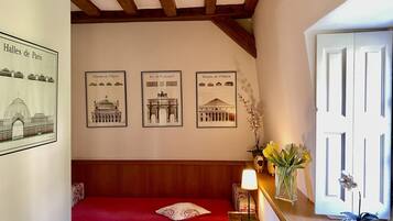 Quarto com cama vermelha, mesa de cabeceira com abajur e três quadros com imagens de pontos turísticos parisienses na parede.