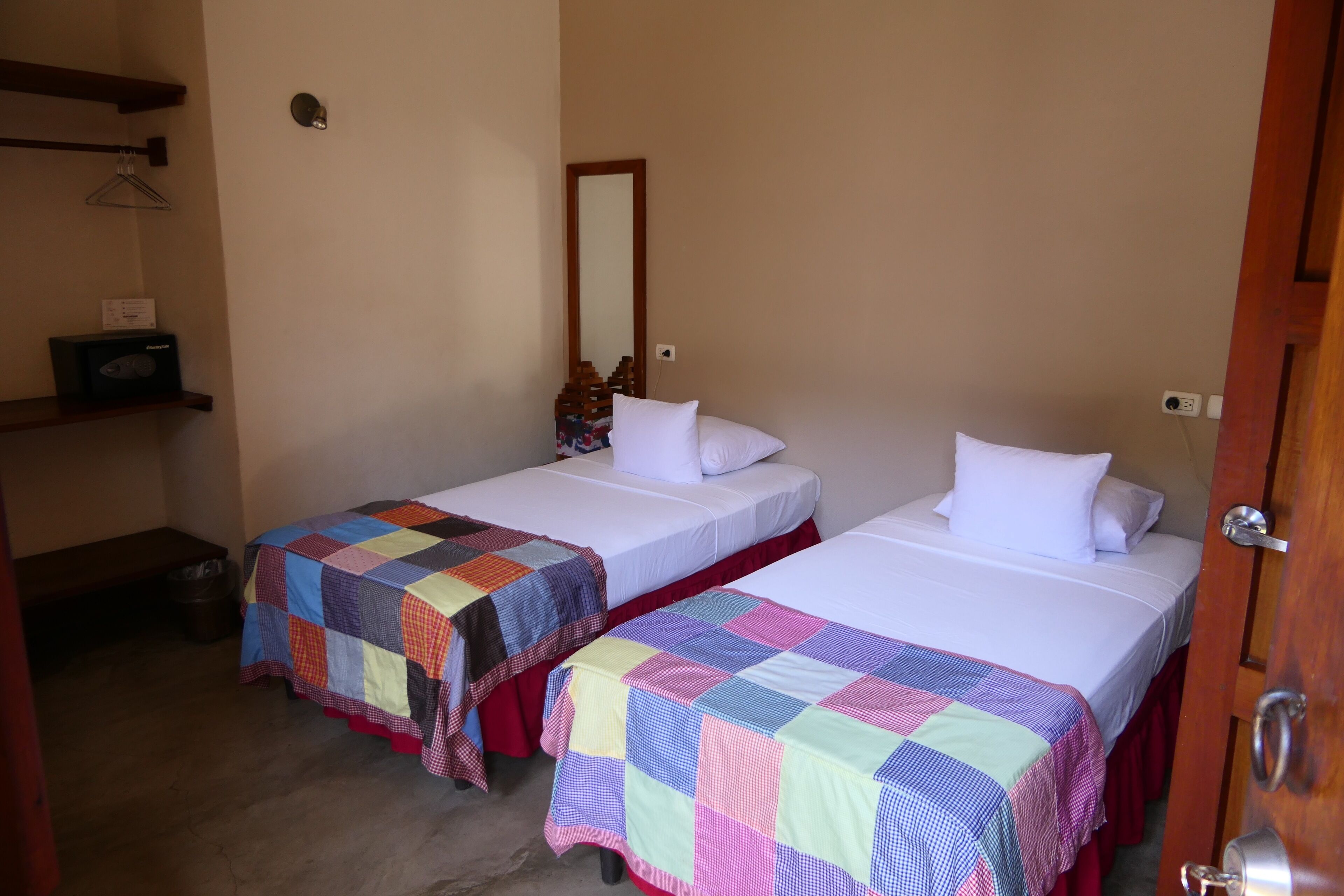 Quarto com duas camas, cada uma com um edredom colorido, uma prateleira de madeira com um rádio e um espelho na parede.