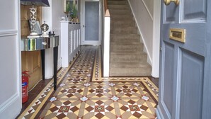 Um corredor com piso estampado, uma escada e uma porta com puxador de latão.