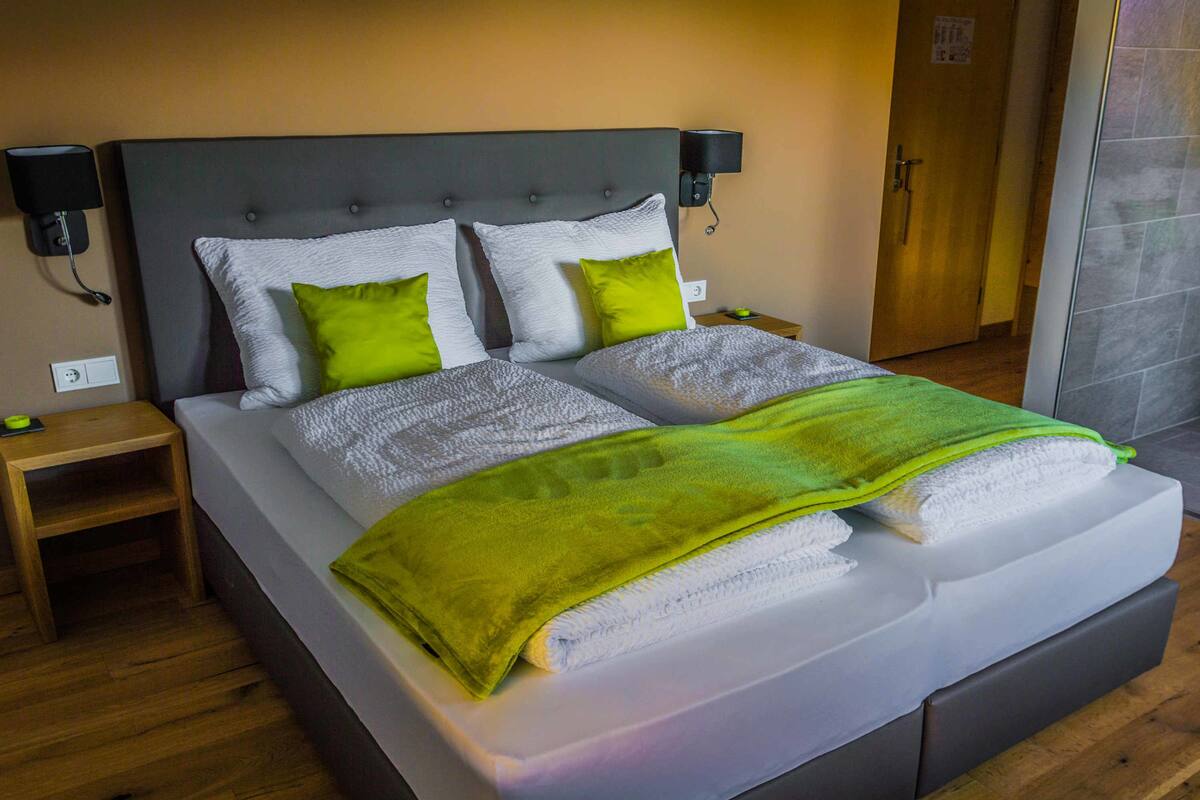 Quarto de hotel moderno com uma cama grande, duas mesinhas de cabeceira e um criado-mudo.
