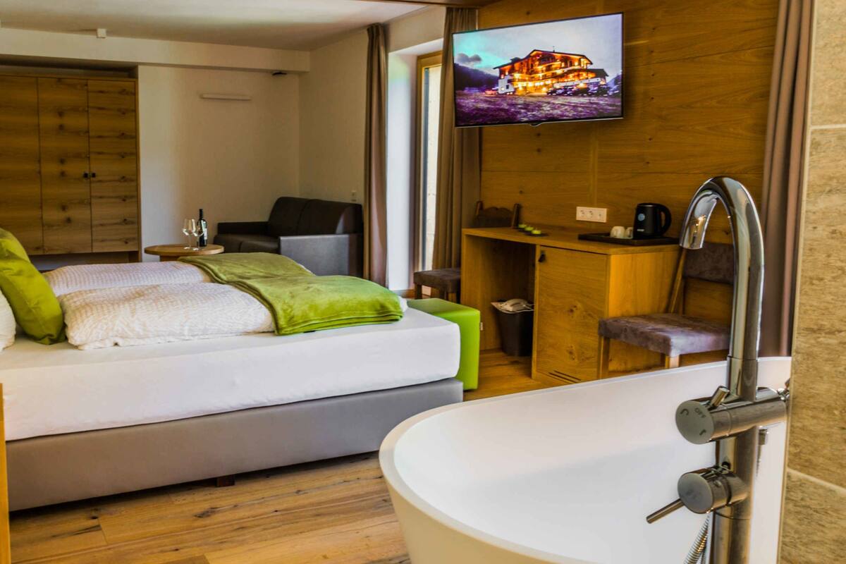 Quarto de hotel moderno com uma cama, televisão fixada na parede, armário de madeira e banheiro com banheira e pia.