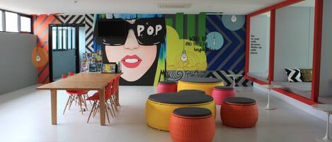 Um espaço de escritório moderno com uma mesa grande, cadeiras coloridas e arte vibrante nas paredes.