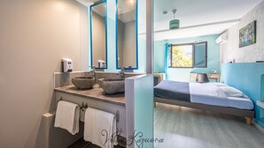 Uma casa de banho moderna com um espelho grande, duas bacias e uma cama no quarto adjacente.