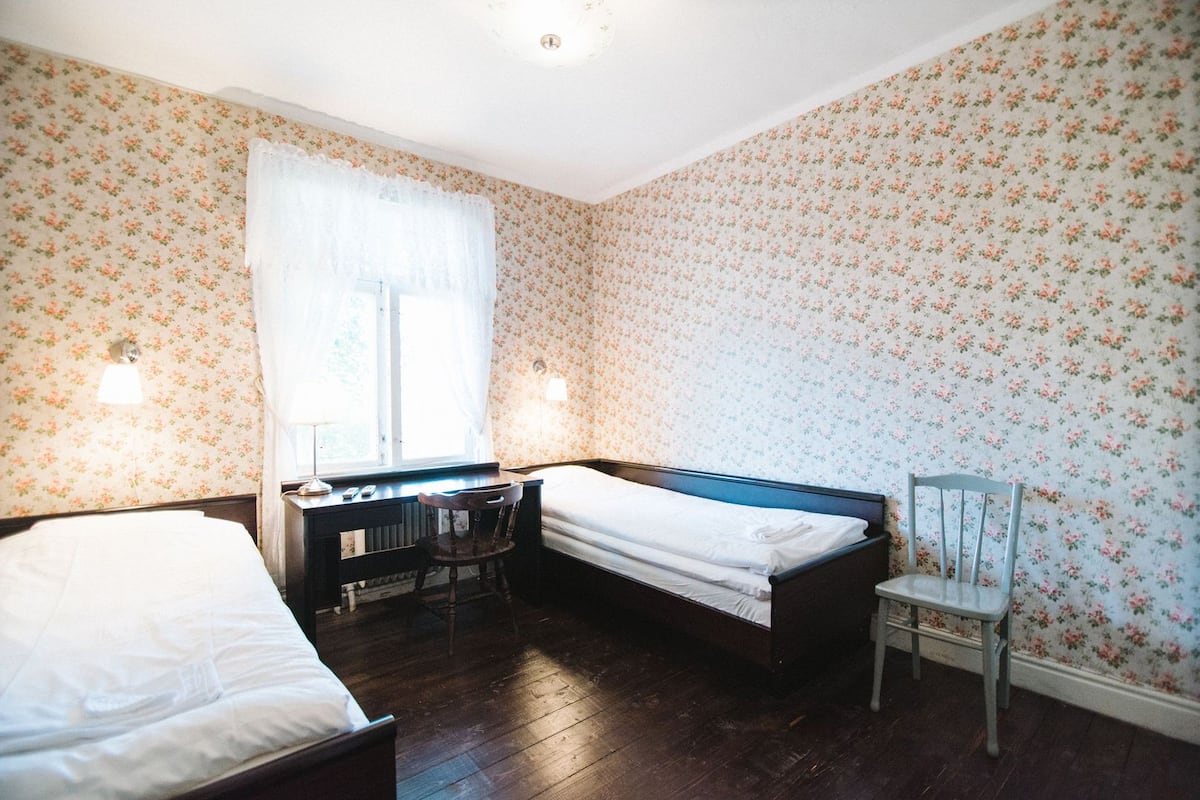 Quarto com duas camas, uma escrivaninha e uma cadeira.