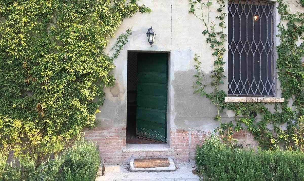 Um edifício com porta verde, um pequeno degrau que leva à entrada, e uma janela com grades de metal.
