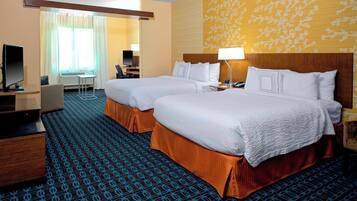 Quarto de hotel com duas camas, uma escrivaninha, uma cadeira, televisão e janela com cortinas.
