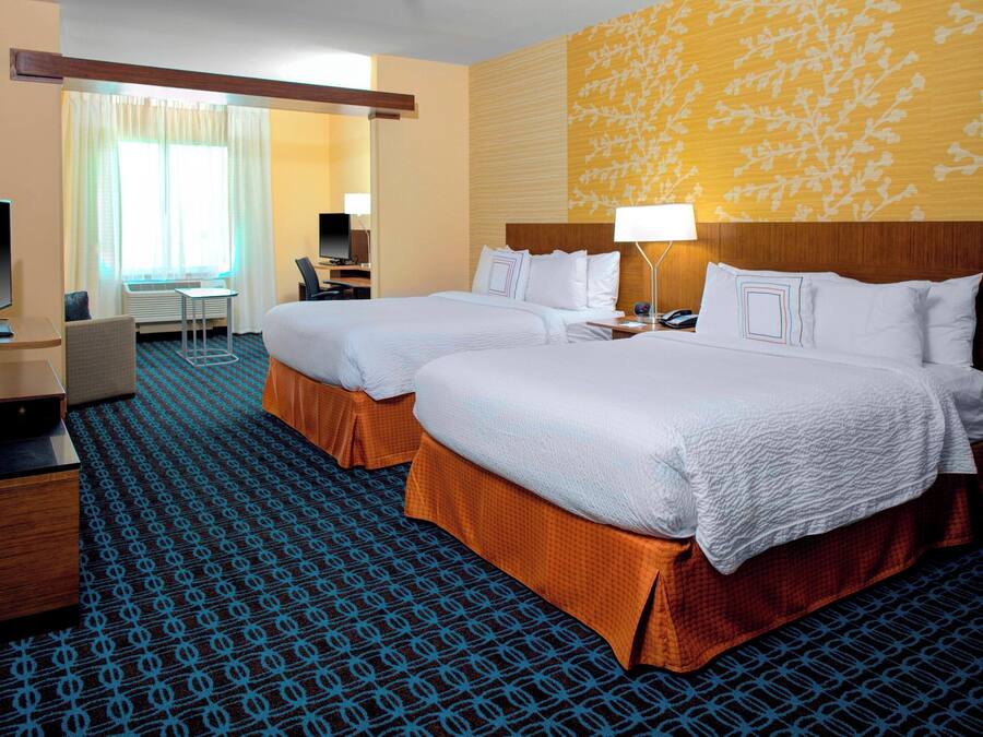 Quarto de hotel com duas camas, uma escrivaninha, uma cadeira, televisão e janela com cortinas.